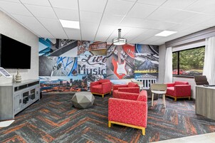 Quarto de hotel com mural da paisagem urbana, sofás estampados em vermelho, uma escrivaninha e uma televisão.