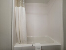 Uma banheira branca com cortina de chuveiro em um banheiro com paredes e piso revestidos de branco.