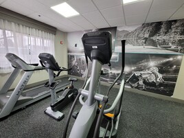 Uma academia com esteiras e bicicletas ergométricas, um espelho grande e um cartaz motivacional na parede.