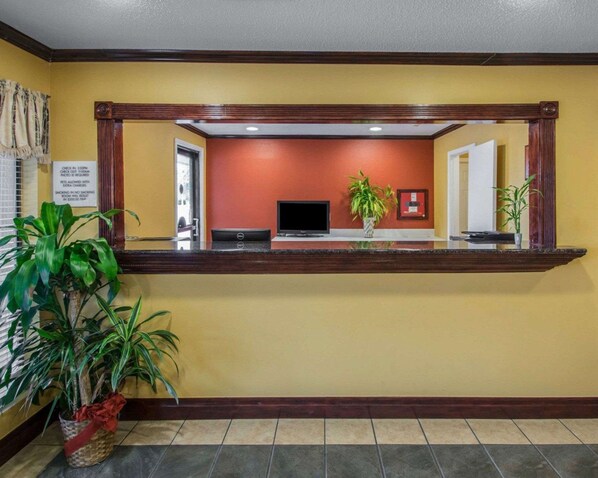 Uma área de recepção com balcão de check-in, televisão e plantas em vasos.
