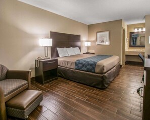 Quarto de hotel com cama, duas mesas de cabeceira com abajures, uma cadeira, escrivaninha e espelho.