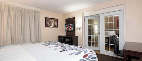 Quarto de hotel com uma cama grande, uma escrivaninha, uma cadeira, televisão e uma porta de vidro deslizante para o exterior.
