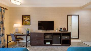 Quarto de hotel com escrivaninha, cadeira, televisão, minibar e um espelho grande.