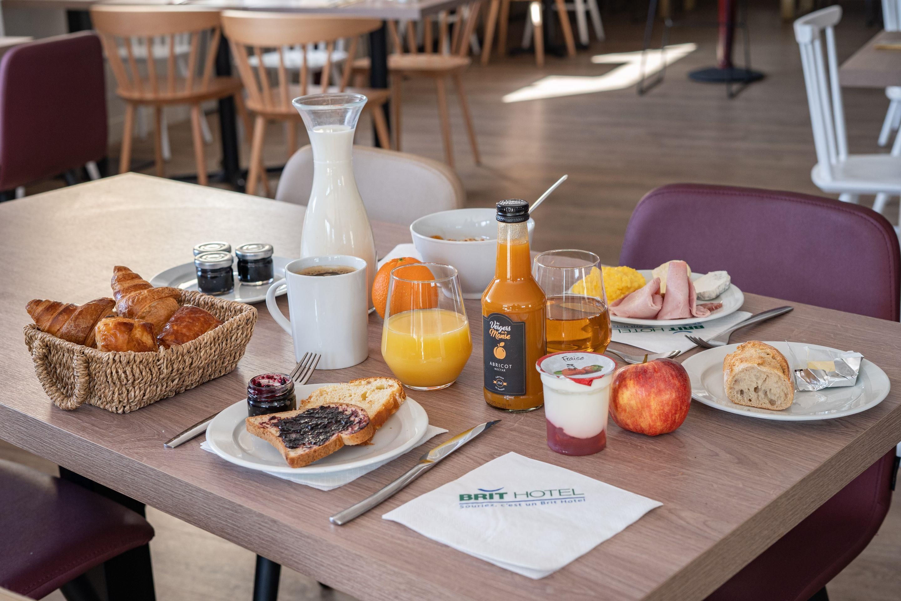 Mesa de café da manhã com croissants, geleia, suco e uma garrafa de suco de laranja.