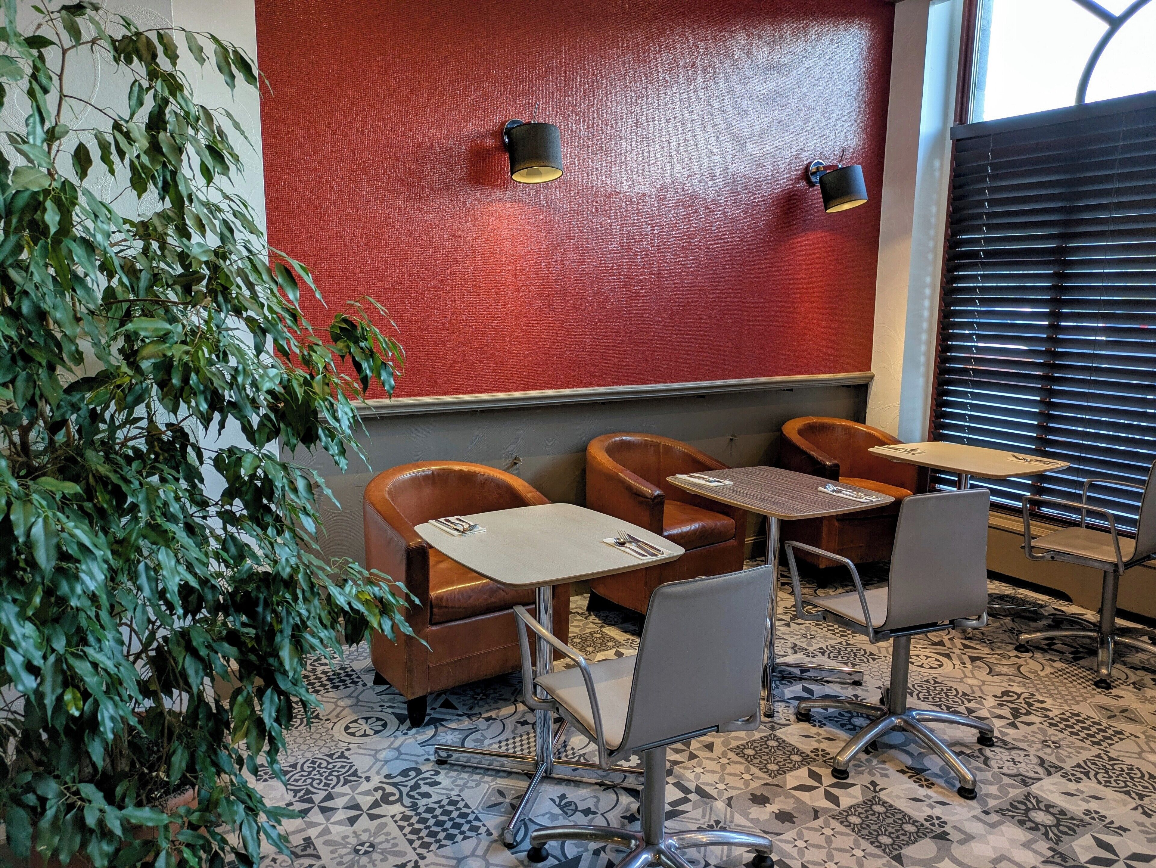 Uma área de estar com poltronas de couro, mesas, um vaso de planta e uma parede texturizada vermelha.