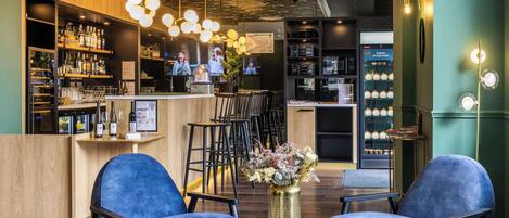 Uma área de bar com balcão de madeira, cadeiras estofadas azuis, uma mesa redonda com um vaso e um teto com luminárias pendentes.