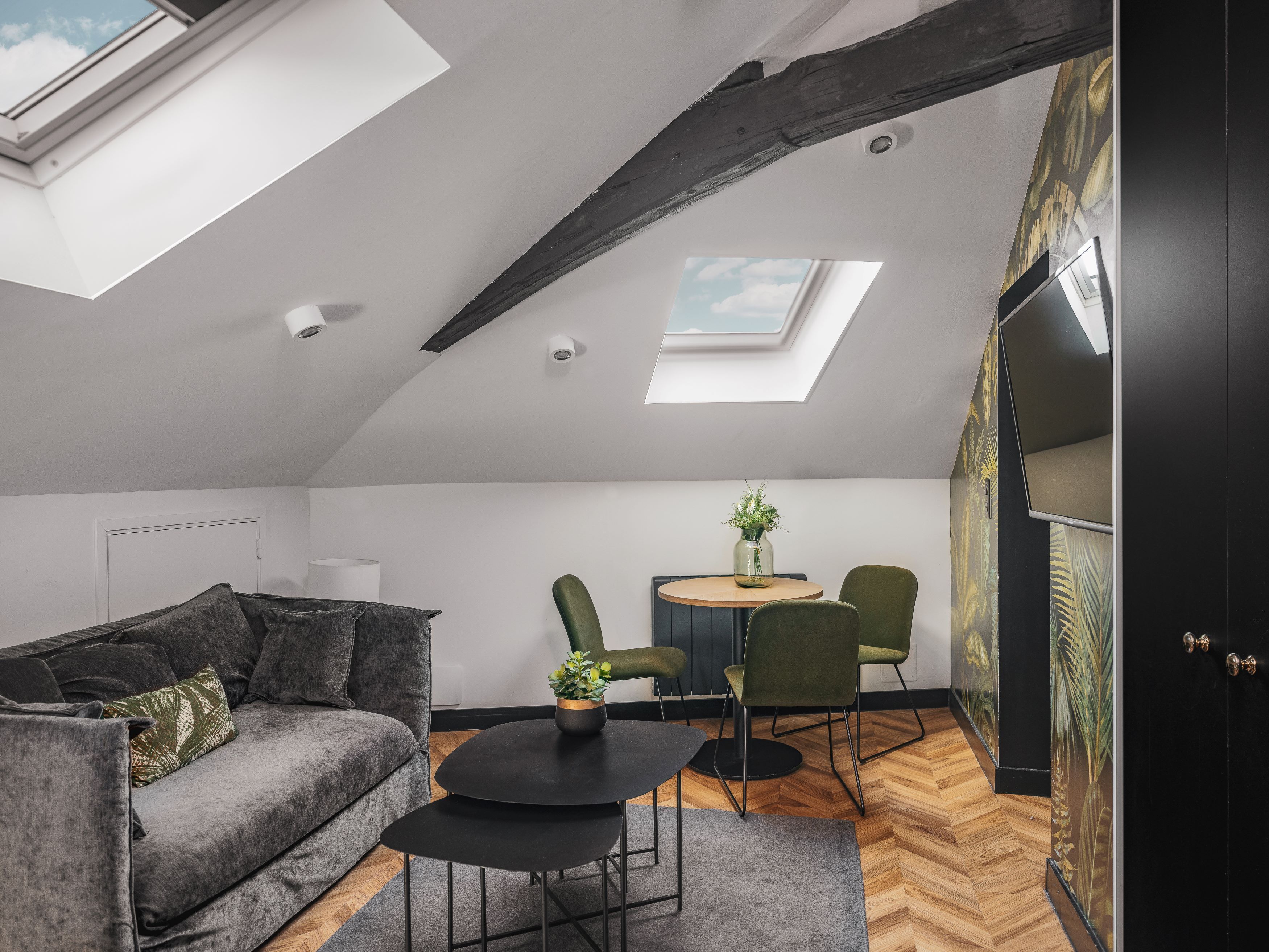 Um apartamento moderno estilo loft com pé direito alto, claraboias, uma área de estar aconchegante com sofá e poltronas, uma pequena mesa redonda e uma lareira.