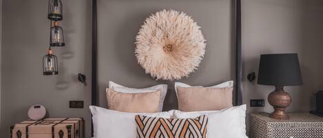 Quarto moderno com cama, almofadas decorativas, um enfeite de parede fofo, luminária e mesa de cabeceira.