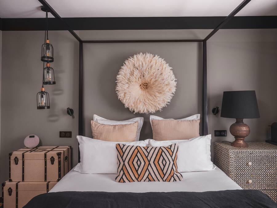 Quarto moderno com cama, almofadas decorativas, um enfeite de parede fofo, luminária e mesa de cabeceira.