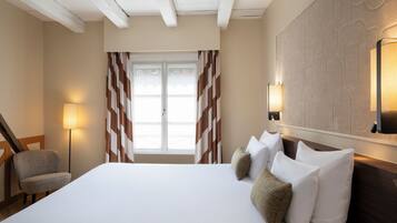 Quarto de hotel com uma cama grande, uma cadeira, um abajur e uma janela com cortinas.