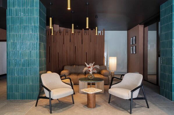 Uma área de estar moderna com um sofá, duas poltronas, uma mesa de centro e iluminação pendente.
