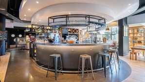 Uma área de bar moderna com um balcão curvo, banquetas e uma variedade de garrafas e copos.