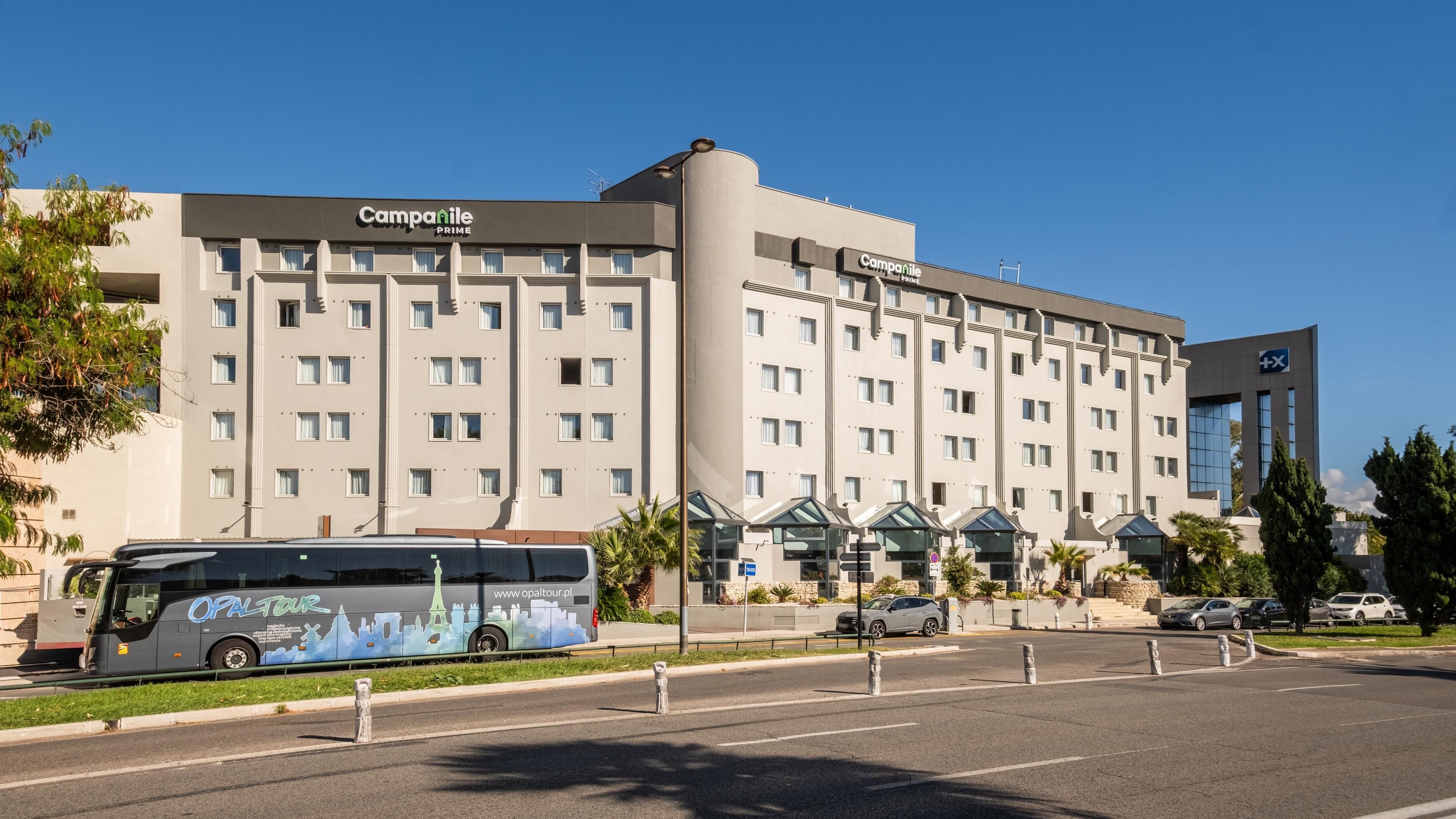Um hotel grande com vários andares, um letreiro de 'Campanile Prime' em destaque e um símbolo 'Plus' indicando comodidades adicionais.