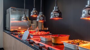 Buffet com diversos alimentos e um eletrodoméstico de aço inoxidável ao fundo.