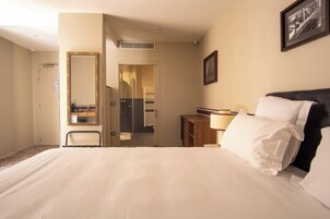 Quarto de hotel com cama, escrivaninha, cadeira, espelho, guarda-roupa e um quadro na parede.