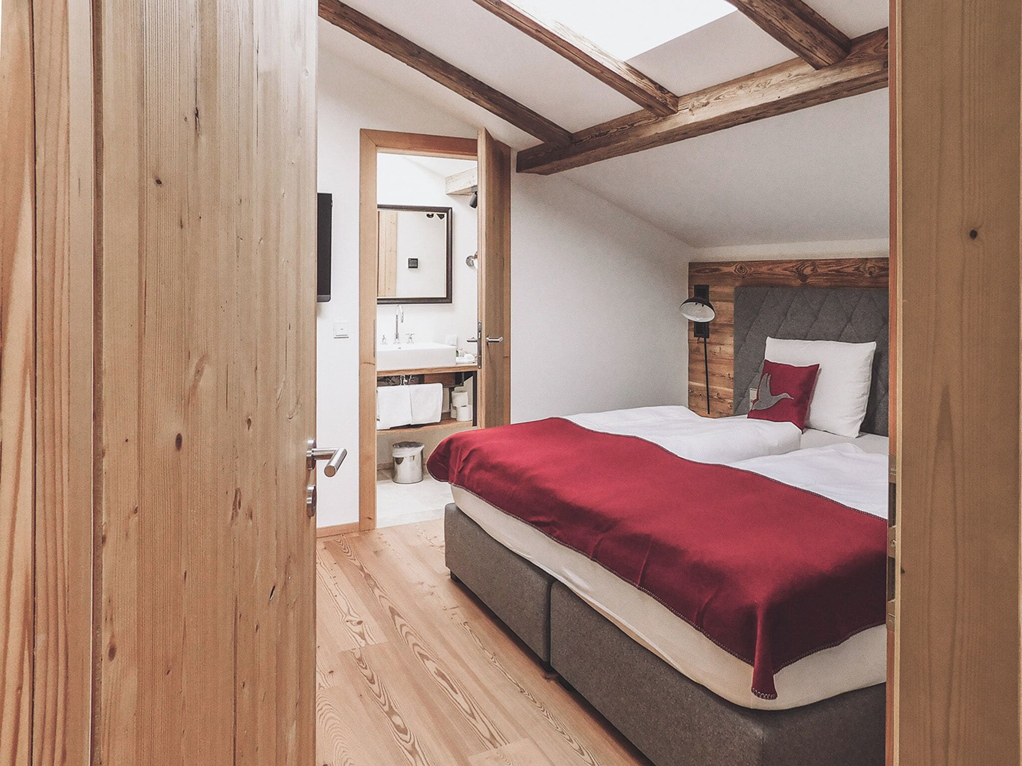 Quarto com cama, teto de madeira, banheiro pequeno e chão de madeira.