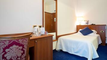 Quarto de hotel com cama, mesa de cabeceira de madeira, espelho e escrivaninha com cadeira.