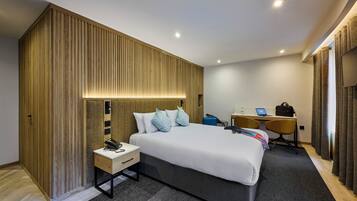 Quarto de hotel moderno com uma cama grande, uma escrivaninha com um laptop e um guarda-roupa.