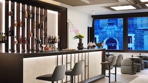Uma área de bar com design moderno, apresentando um balcão com várias garrafas, um vaso com flores e banquetas.