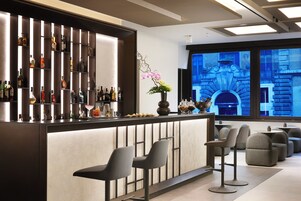Uma área de bar com design moderno, apresentando um balcão com várias garrafas, um vaso com flores e banquetas.
