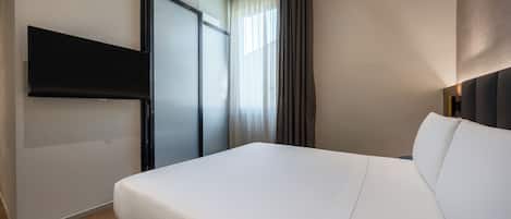 Quarto de hotel com uma cama grande, televisão de tela plana na parede, porta de correr e janela com cortinas.