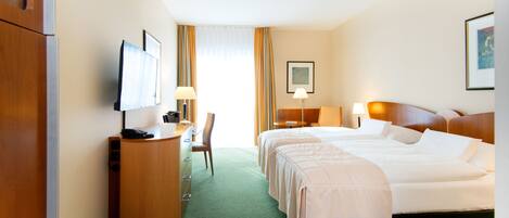 Quarto de hotel com duas camas, uma escrivaninha com telefone, uma cadeira e uma televisão na parede.