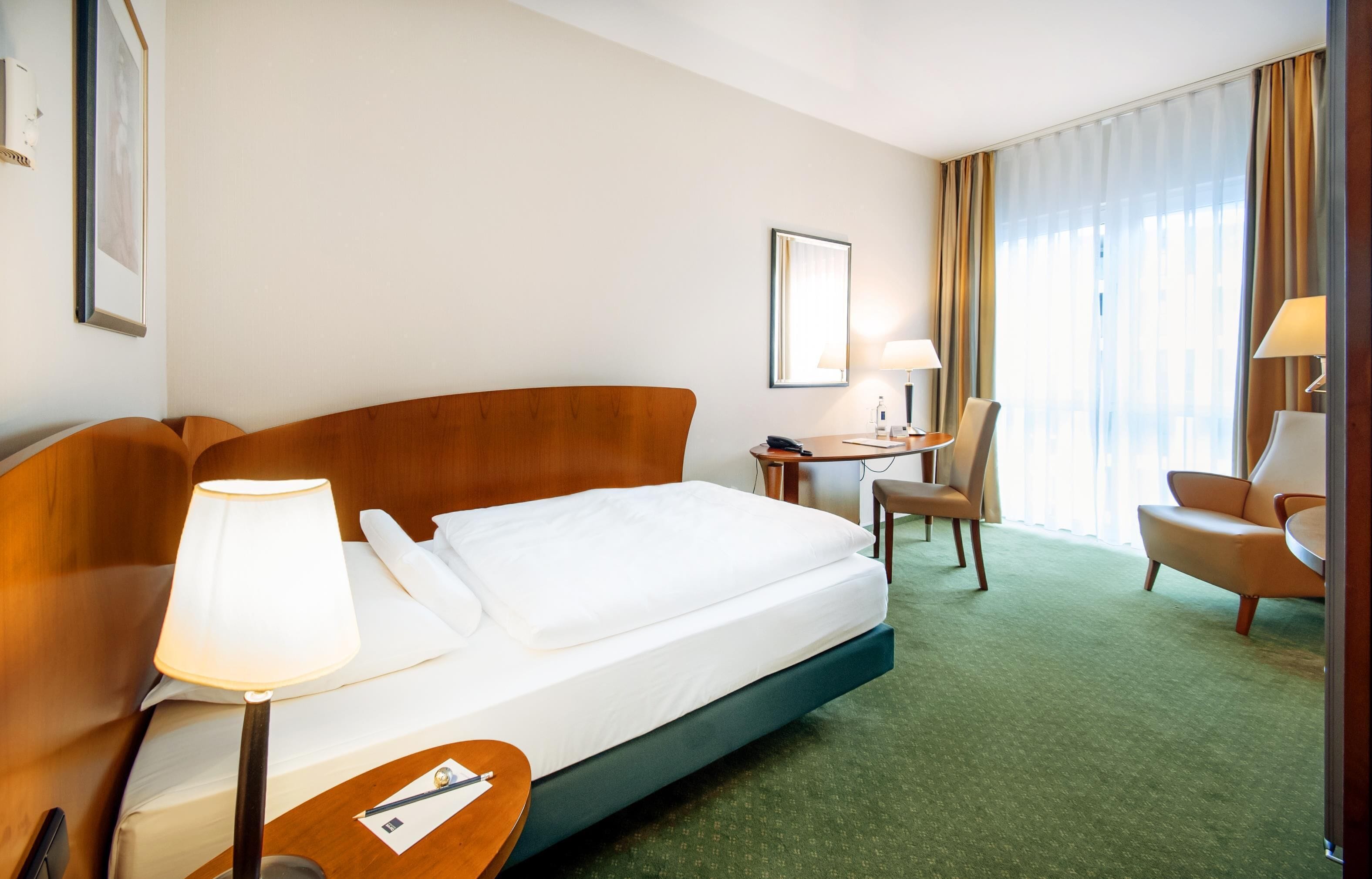 Quarto de hotel com uma cama grande, uma escrivaninha, uma cadeira e um abajur.