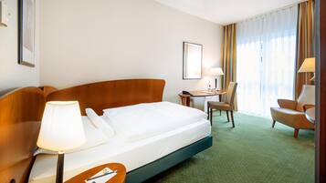 Quarto de hotel com uma cama grande, uma escrivaninha, uma cadeira e um abajur.