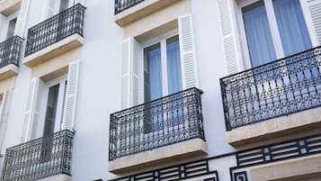 Fachada de edifício com várias varandas, persianas brancas e grades de ferro decorativas.