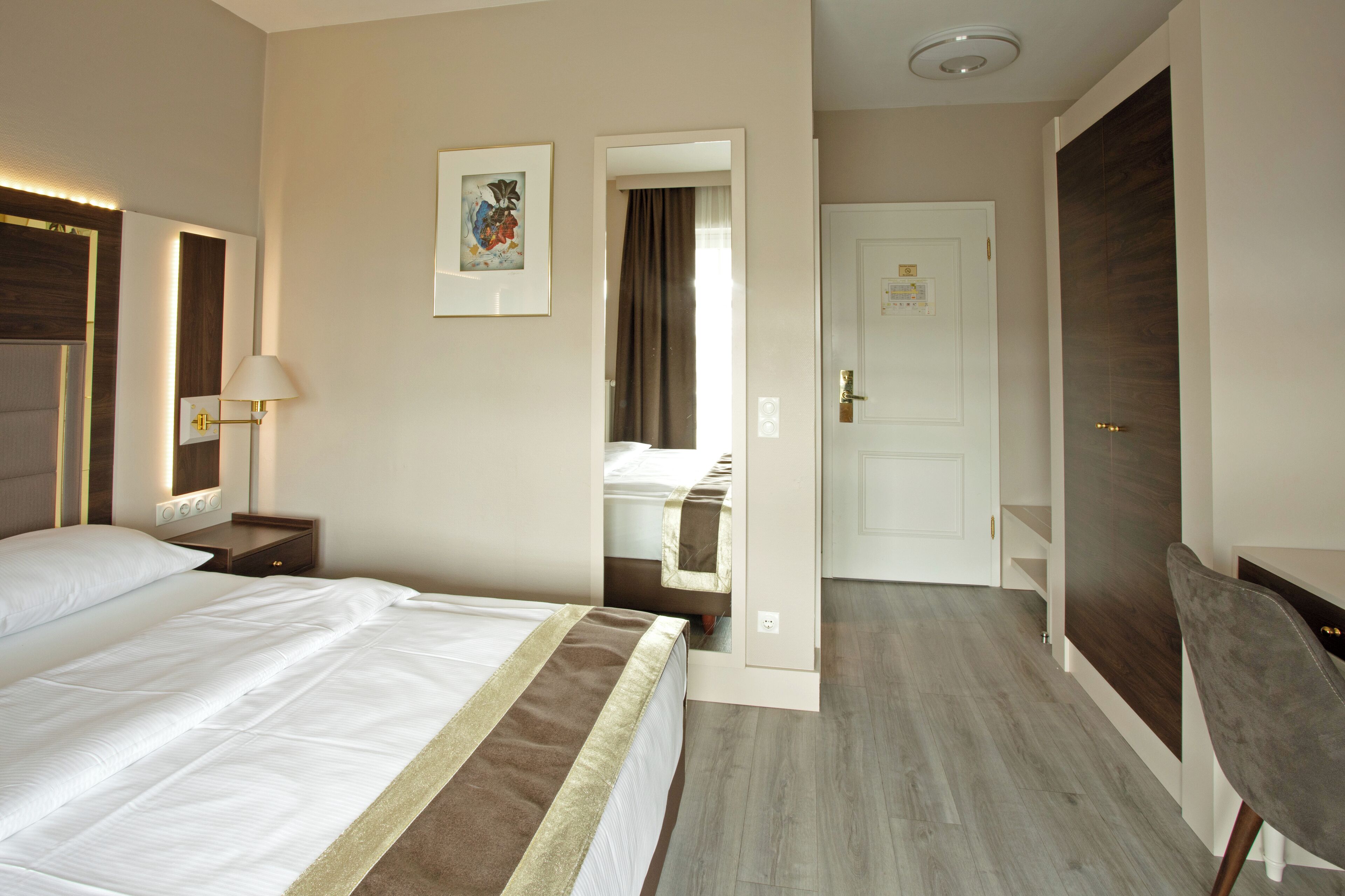 Quarto de hotel com cama, mesa de cabeceira, abajur e espelho.
