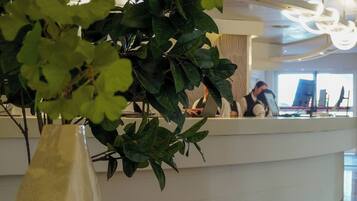 Balcão de recepção com planta em vaso, interior moderno e uma pessoa trabalhando em um computador.