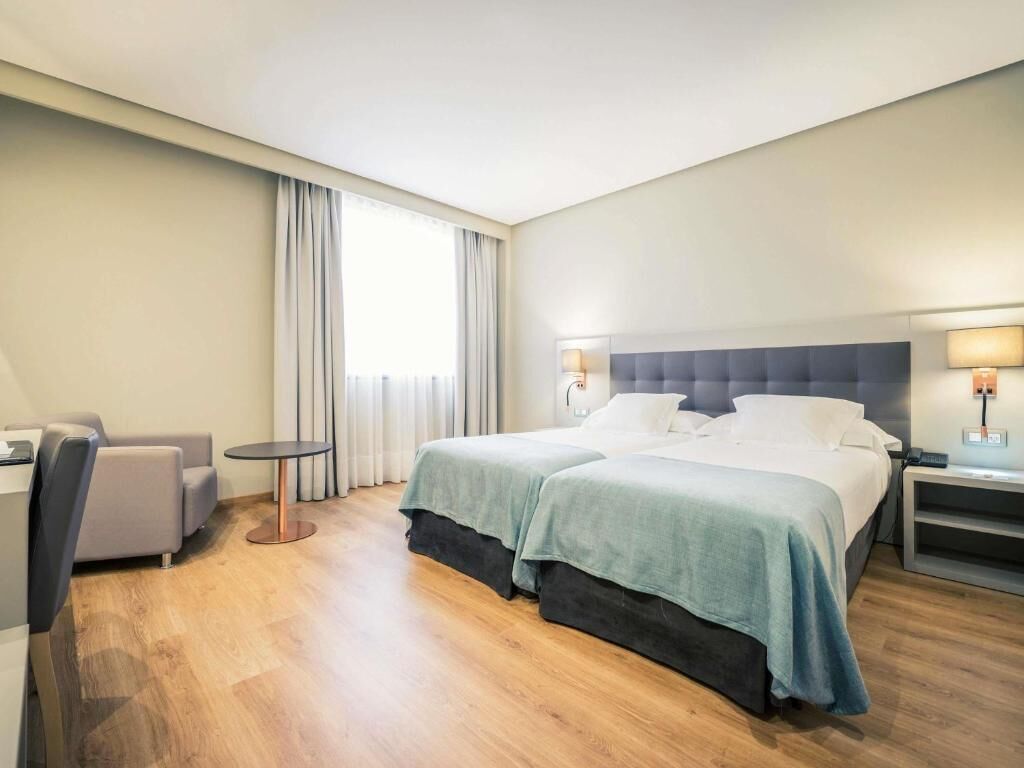 Quarto de hotel com duas camas, um espaço de estar e uma pequena mesa.