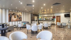 Um saguão de hotel com área de bar, disposição de assentos e uma grande pintura na parede.