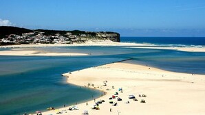 Uma praia costeira com águas cristalinas, areal arenoso e um penhasco ao fundo.