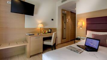 Quarto de hotel com cama, escrivaninha com laptop, TV de tela plana na parede, abajur e espelho.