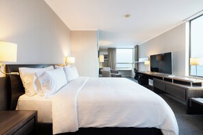 Quarto de hotel com cama grande, escrivaninha e televisão de tela plana, além de vista para o mar pela janela.