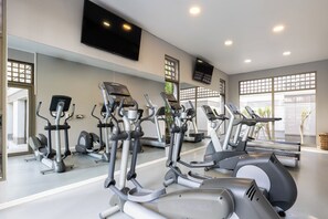 Uma academia com diversos aparelhos de exercício, um espelho grande e uma TV fixada na parede.