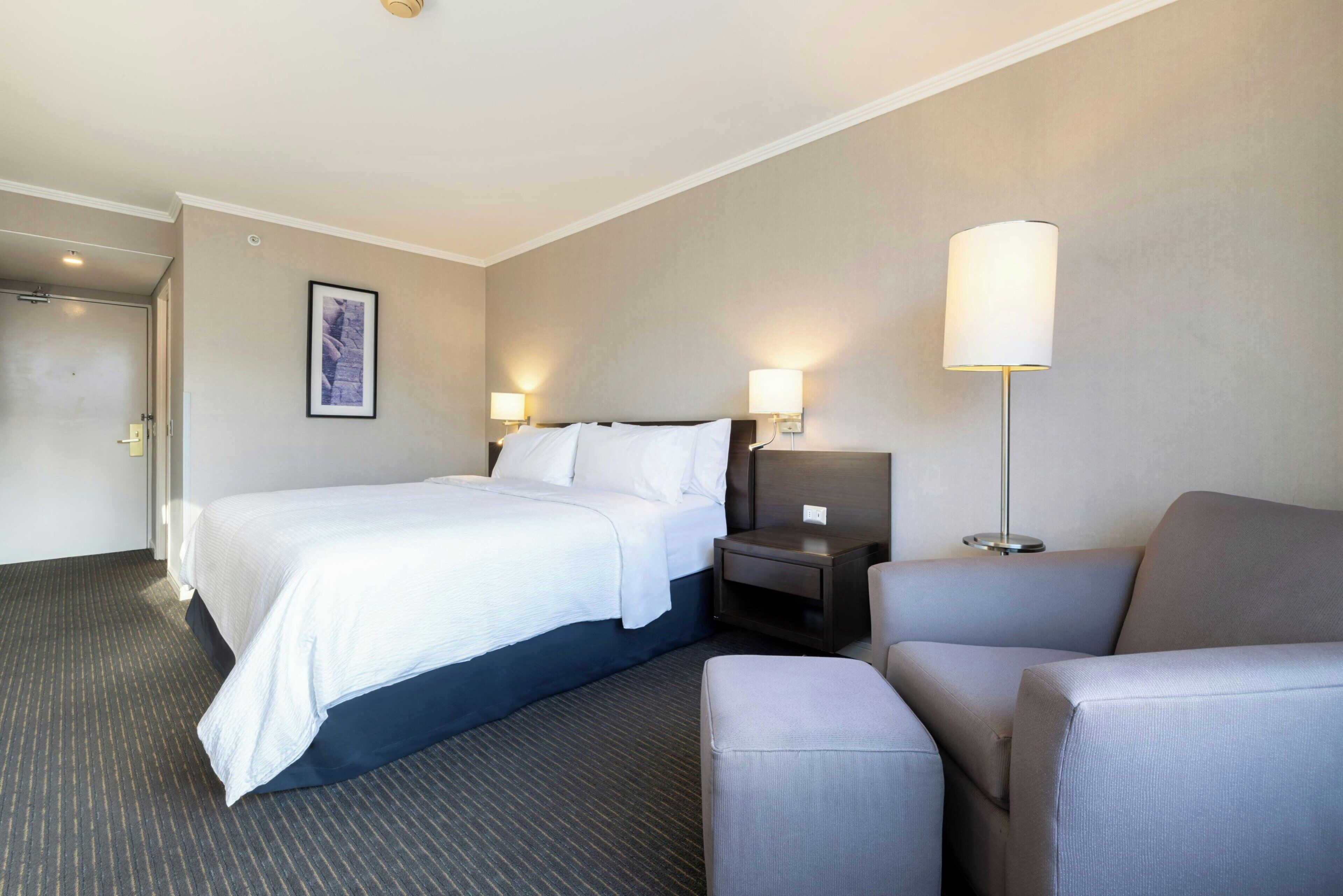 Quarto de hotel com cama, mesa de cabeceira, cadeira e luminária.