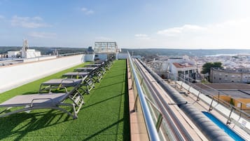 Terraço no telhado com grama sintética verde, espreguiçadeiras e piscina.