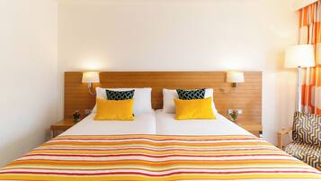 Quarto de hotel com uma cama grande, duas luminárias de cabeceira, um painel de cama de madeira e um edredom listrado.