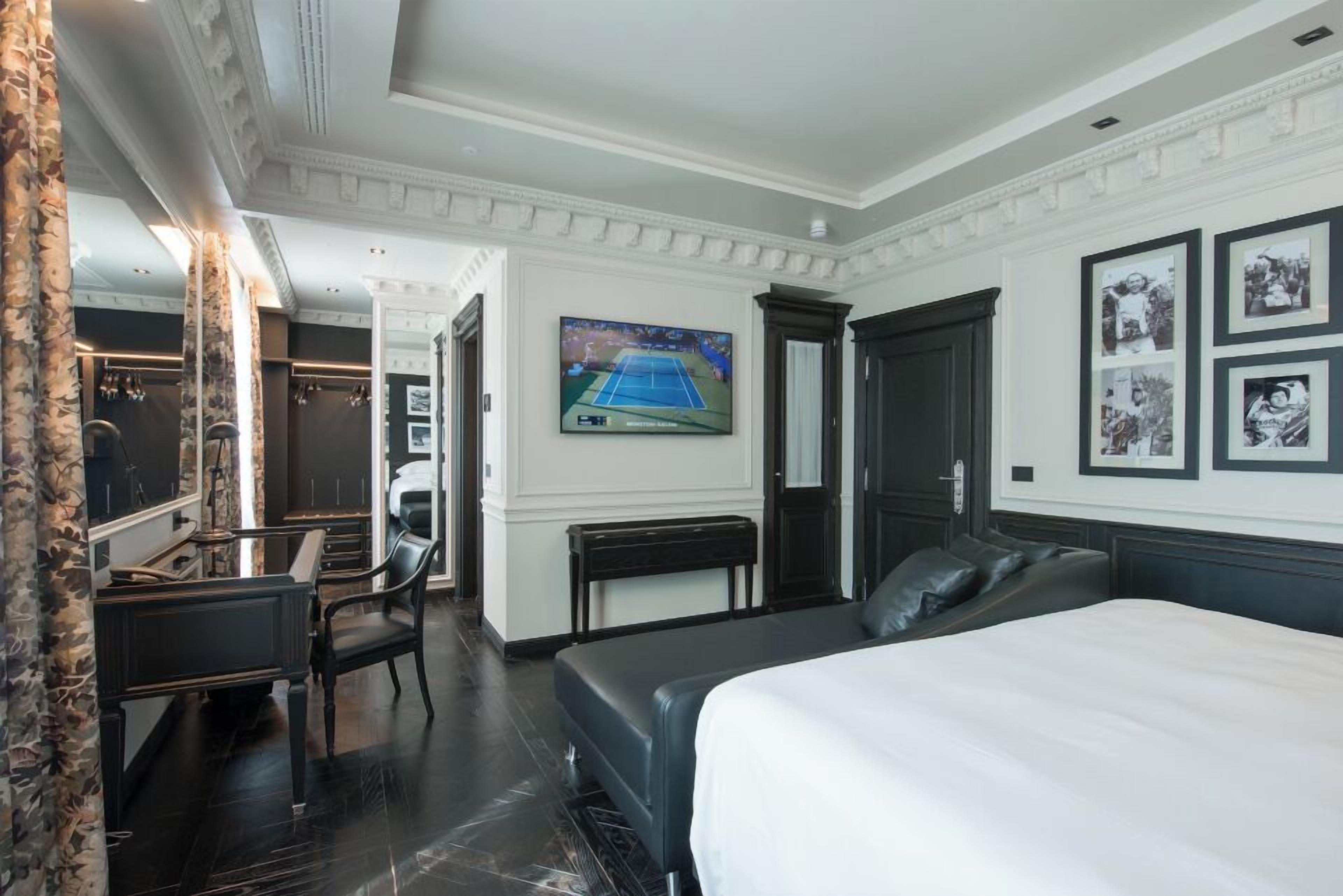 Quarto de hotel com uma cama grande, uma escrivaninha com cadeira, televisão e quadros nas paredes.