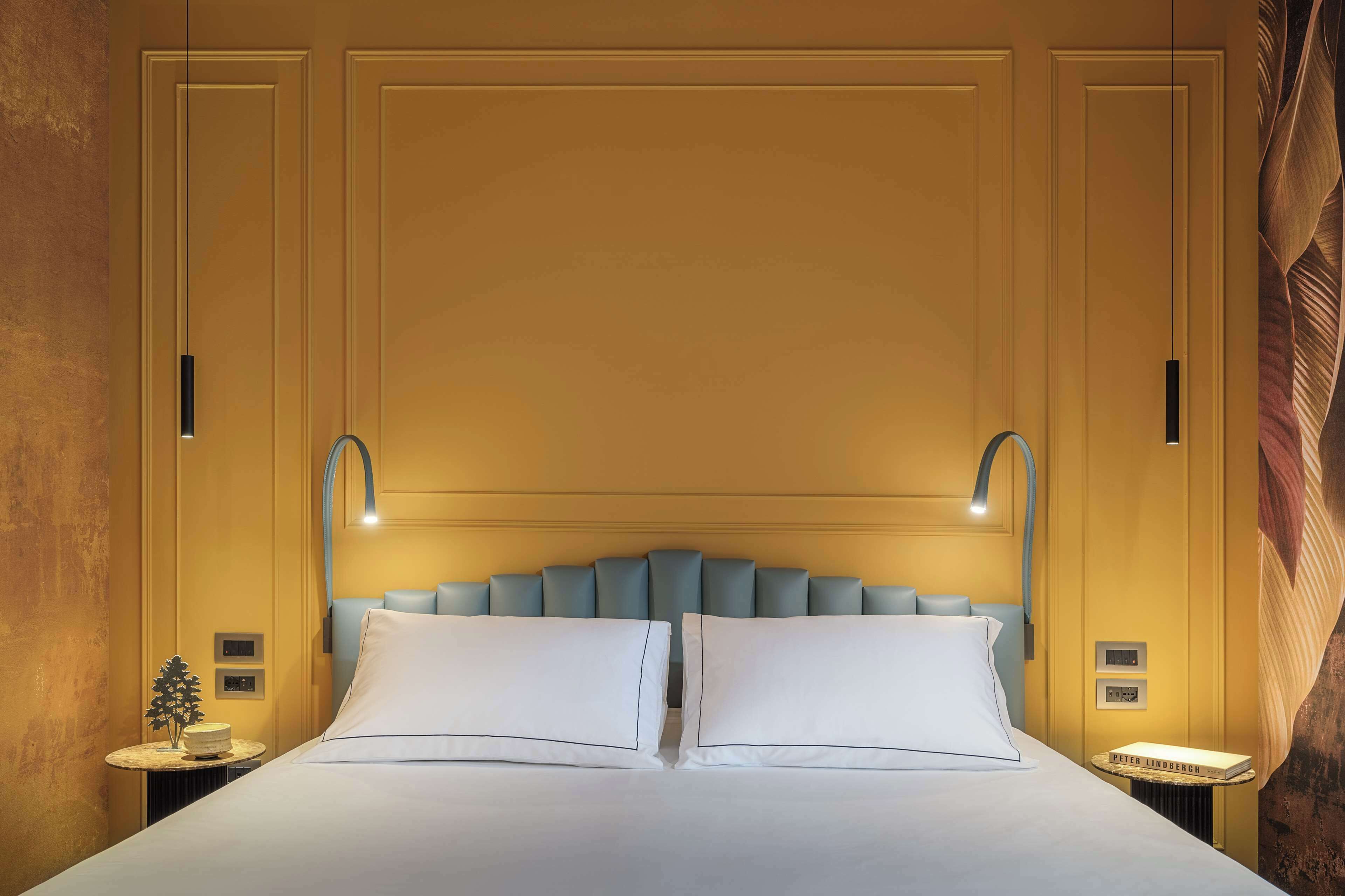 Quarto de hotel com uma cama grande, duas mesas de cabeceira, luminária fixada na parede e painel decorativo.