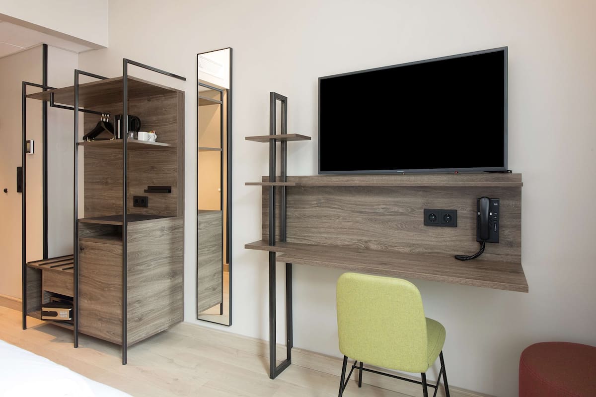 Quarto moderno com televisão integrada, escrivaninha de madeira, cadeira verde e guarda-roupa com espelho.