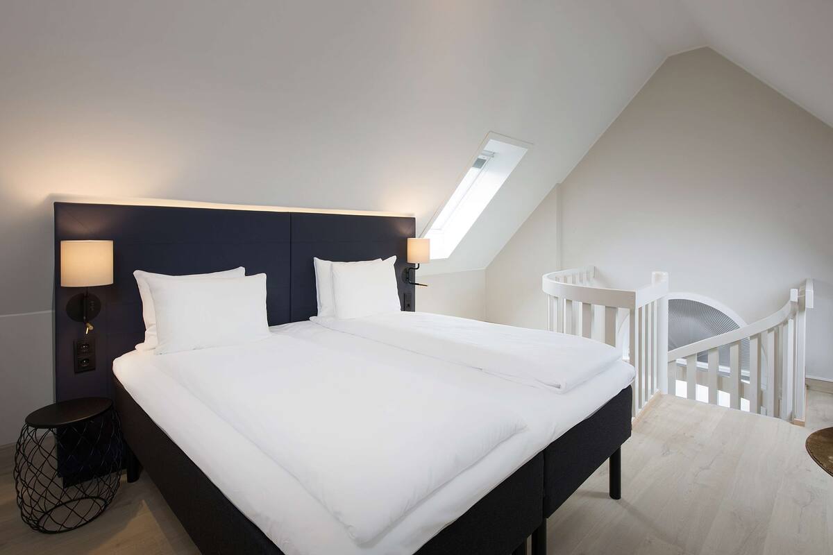 Quarto moderno com uma cama grande, uma mesa de cabeceira, uma luminária e vista para o exterior através de um domo.