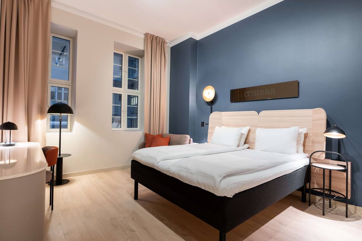 Quarto moderno com cama, mesas de cabeceira, luminária e janela com cortinas.
