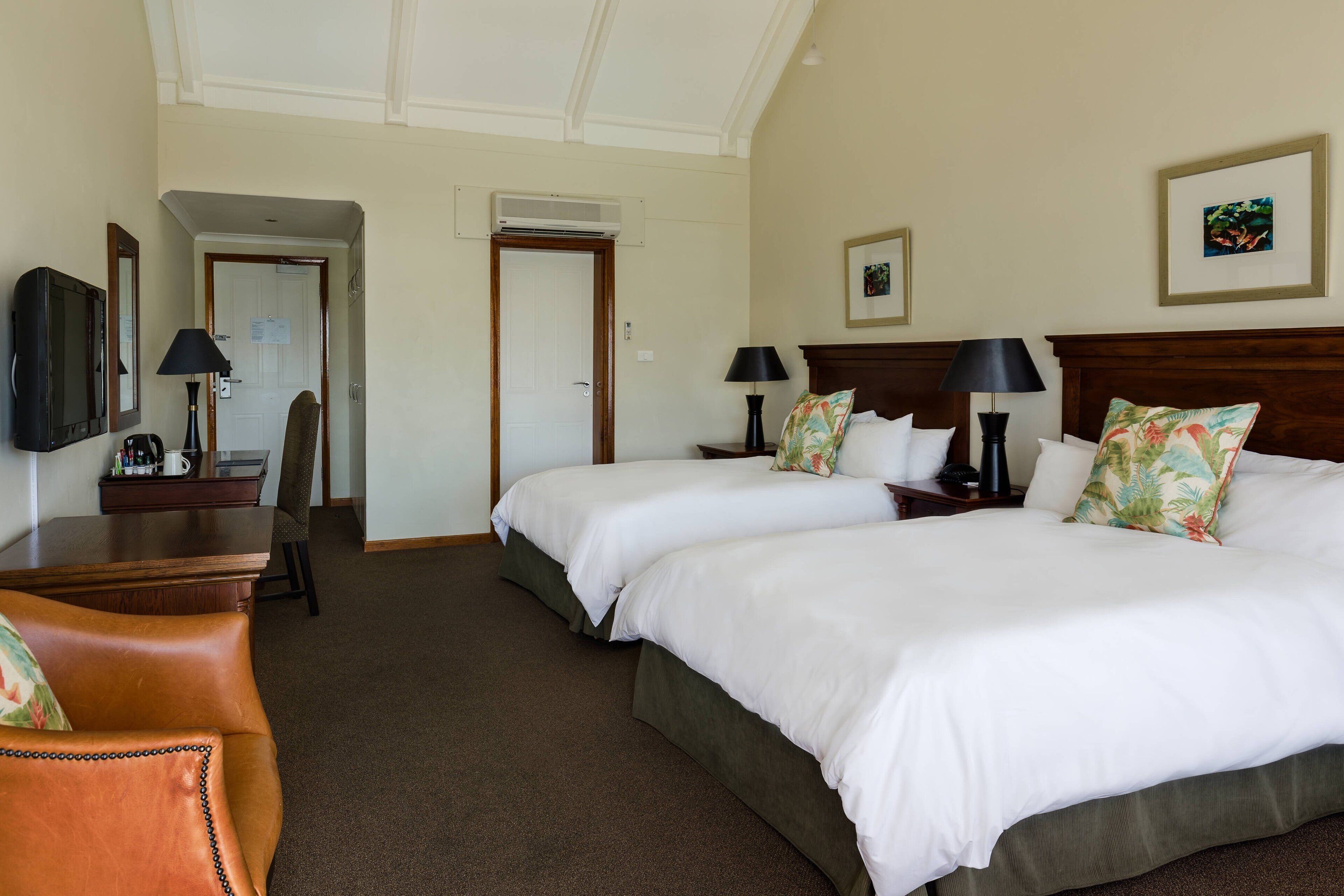Quarto de hotel com duas camas, uma mesa, uma cadeira e uma televisão.