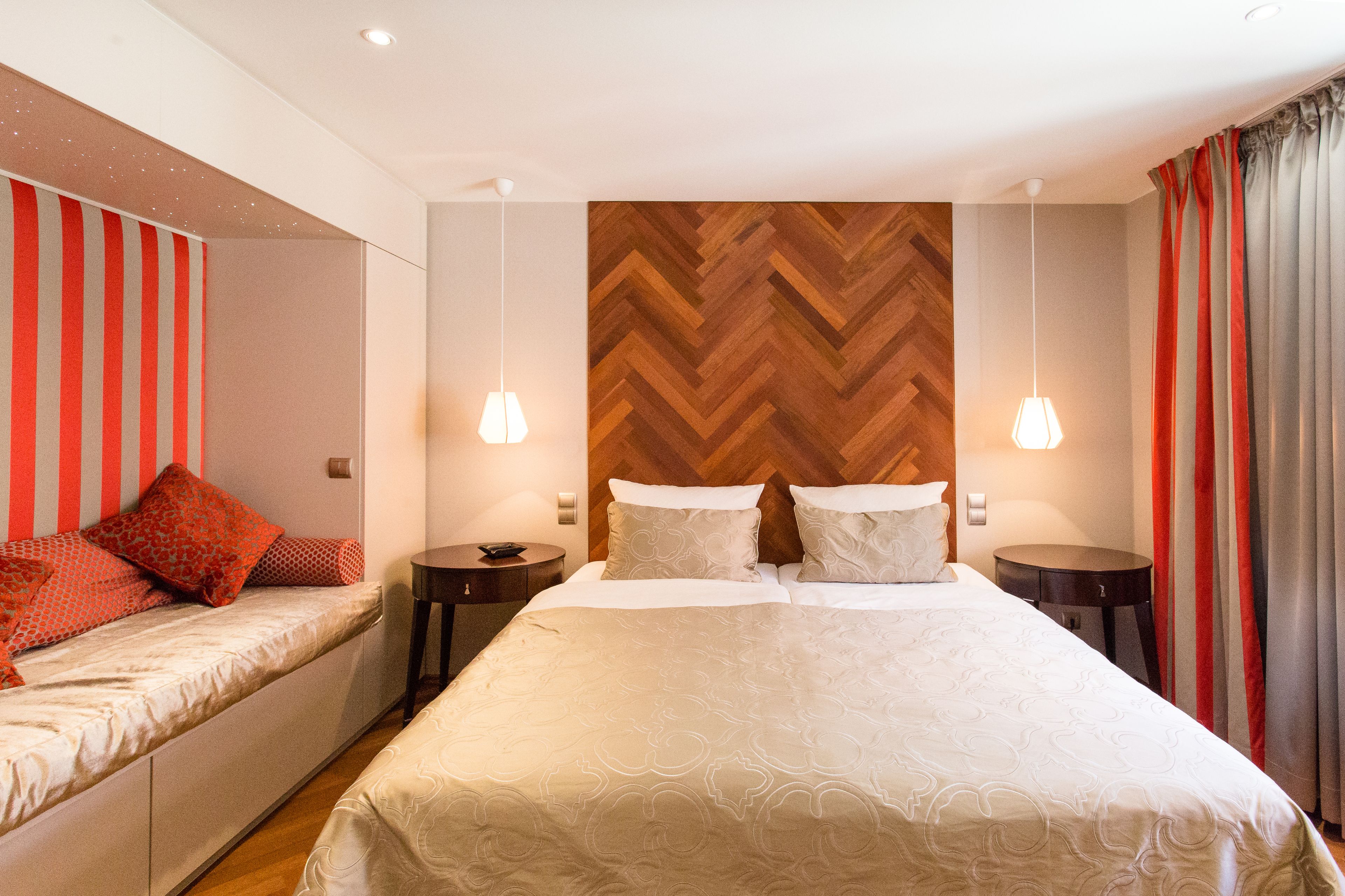 Quarto de hotel com uma cama grande, duas mesas de cabeceira, um espaço de estar pequeno e uma cabeceira de madeira com padrão em espinha de peixe.