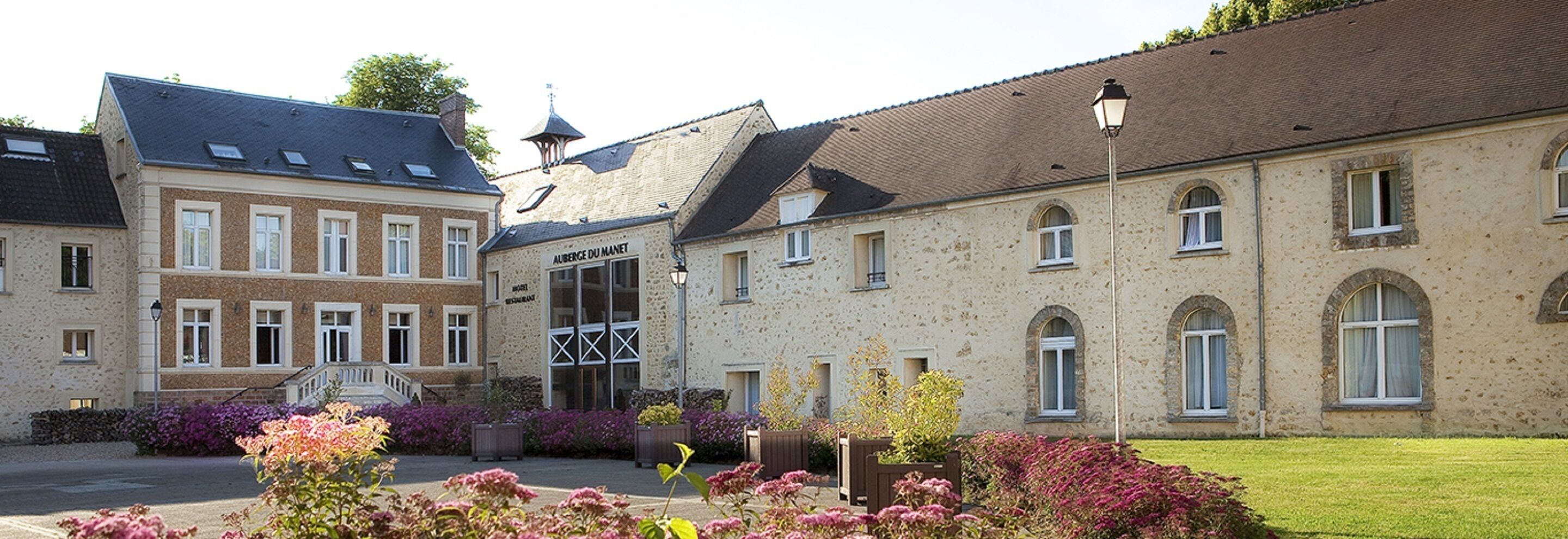 Um pátio com um restaurante chamado "Auberge du Manet" e um edifício com telhado azul.