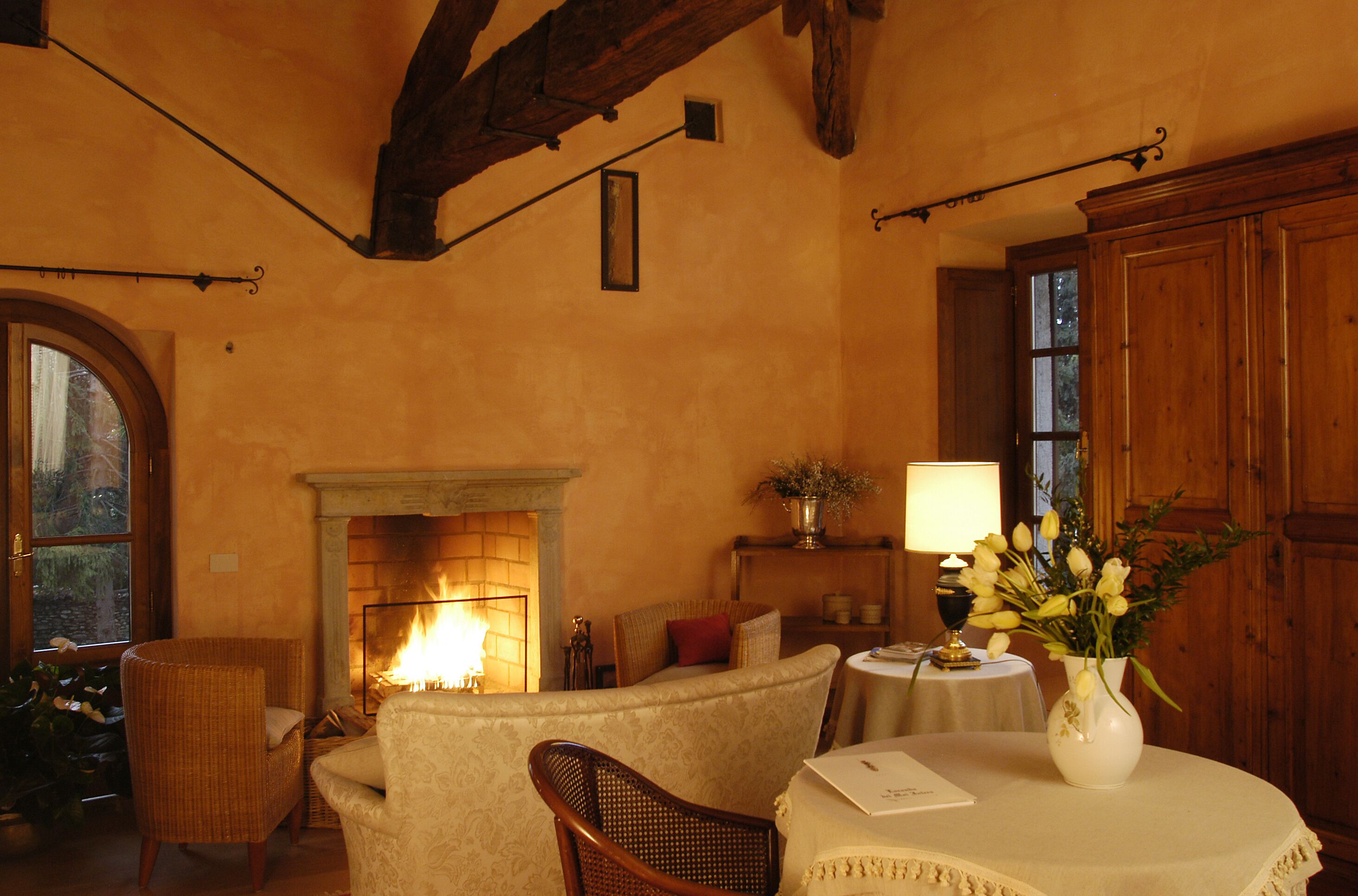 Um quarto aconchegante com lareira, móveis de vime, uma mesa com um vaso de flores e armários de madeira.
