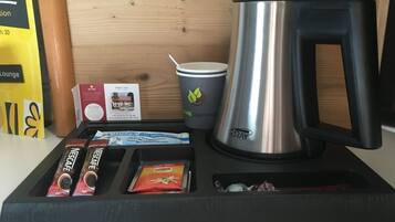Uma cafeteira, uma chávena, uma embalagem de Nescafe e um folheto sobre uma mesa de madeira.